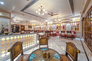 Restaurante com interior tradicional, destacando decorações ornamentais nas paredes, lustres e diferentes opções de assentos.