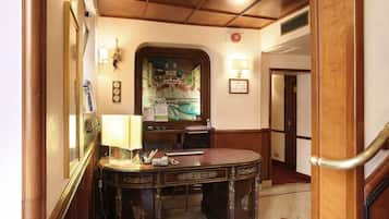 Um hall de hotel com uma mesa de madeira, um espelho, um relógio fixado na parede e um certificado emoldurado.