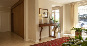 Um corredor com porta de madeira, um console com um vaso e um quadro emoldurado, e um tapete vermelho.