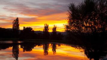 Um lago calmo refletindo um pôr do sol, com árvores e um barco à direita.