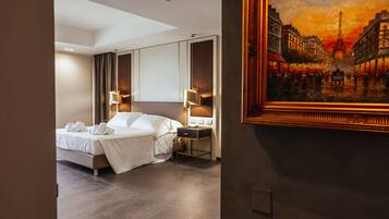 Quarto de hotel moderno com uma cama grande, mesas de cabeceira e uma pintura de uma paisagem urbana.