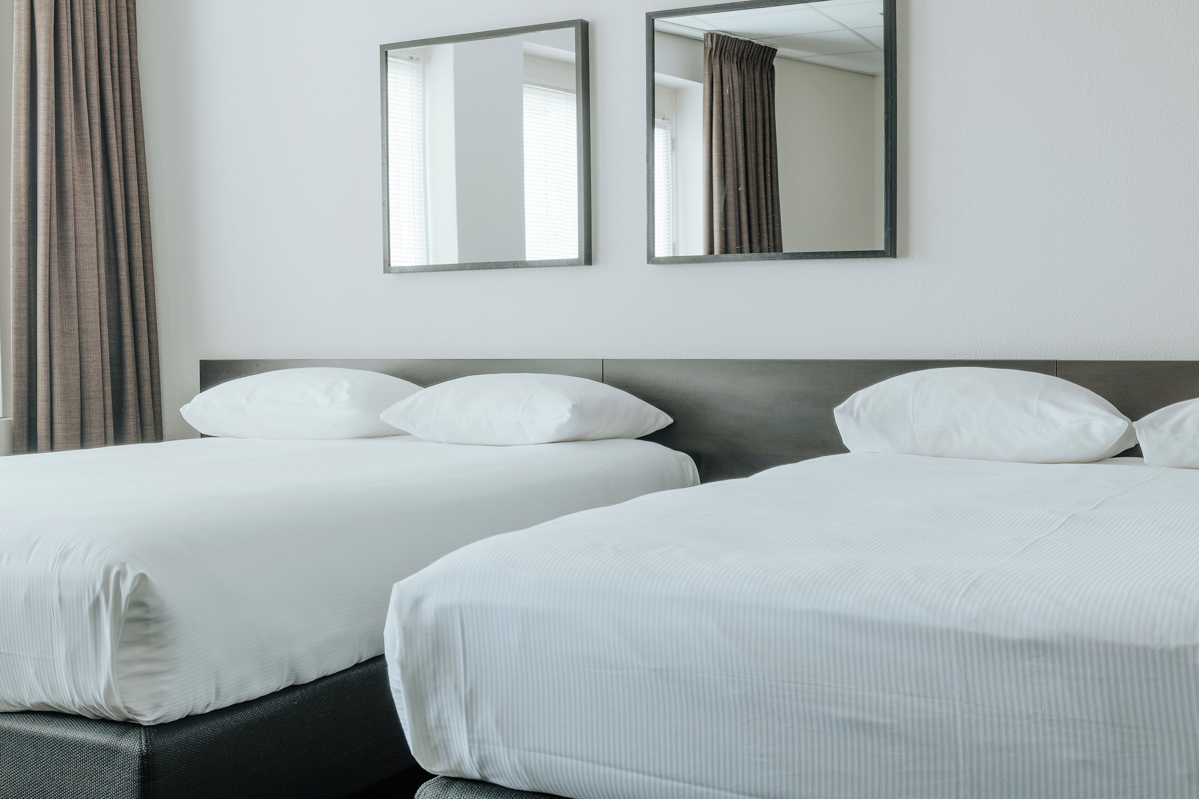 Quarto de hotel com duas camas de solteiro, cabeceira e dois espelhos na parede.