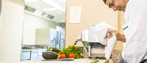 Um chef preparando comida em uma cozinha com um processador de alimentos e vegetais sobre a bancada.