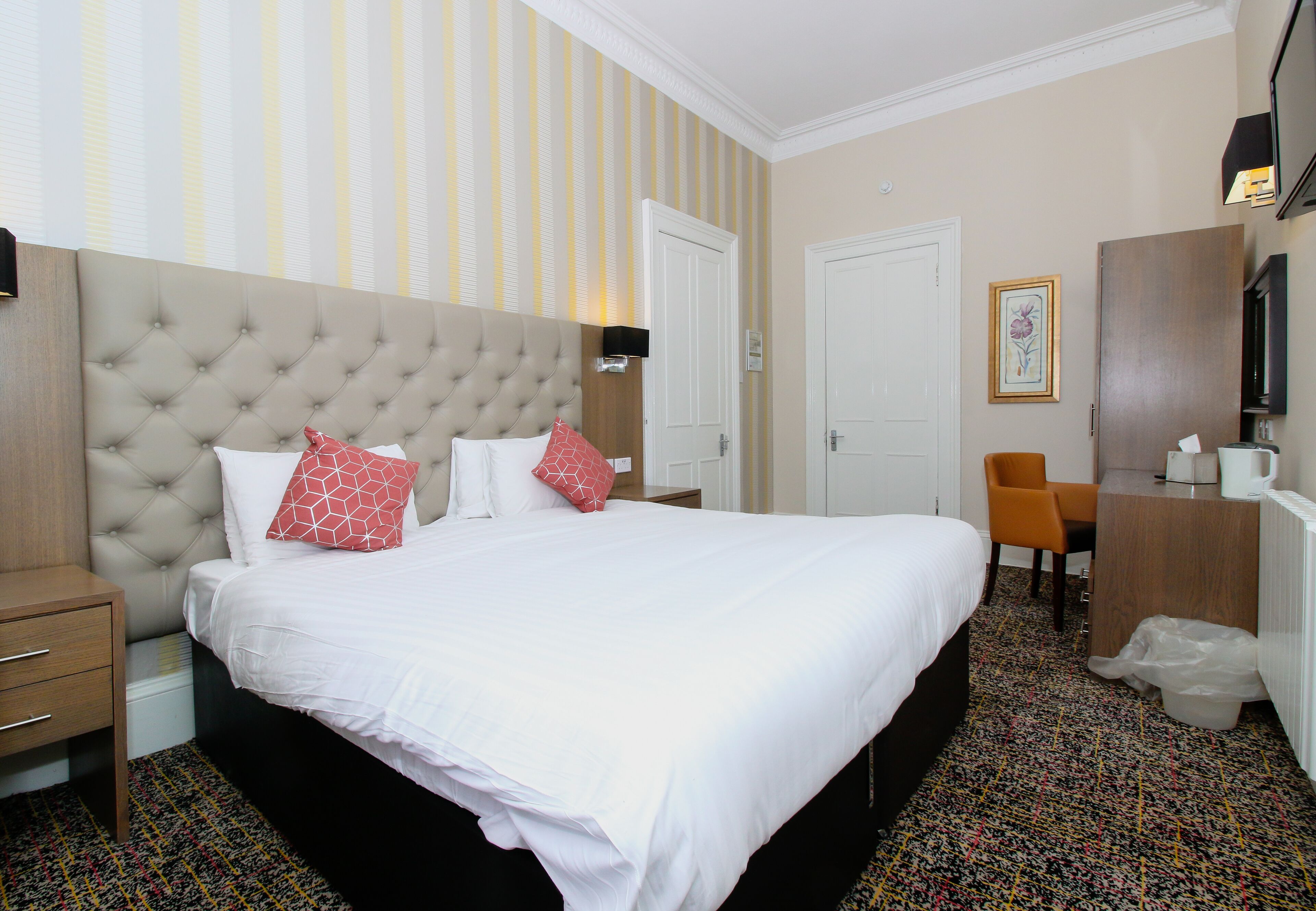 Quarto de hotel com cama grande, mesa de cabeceira, cadeira, escrivaninha e televisão.