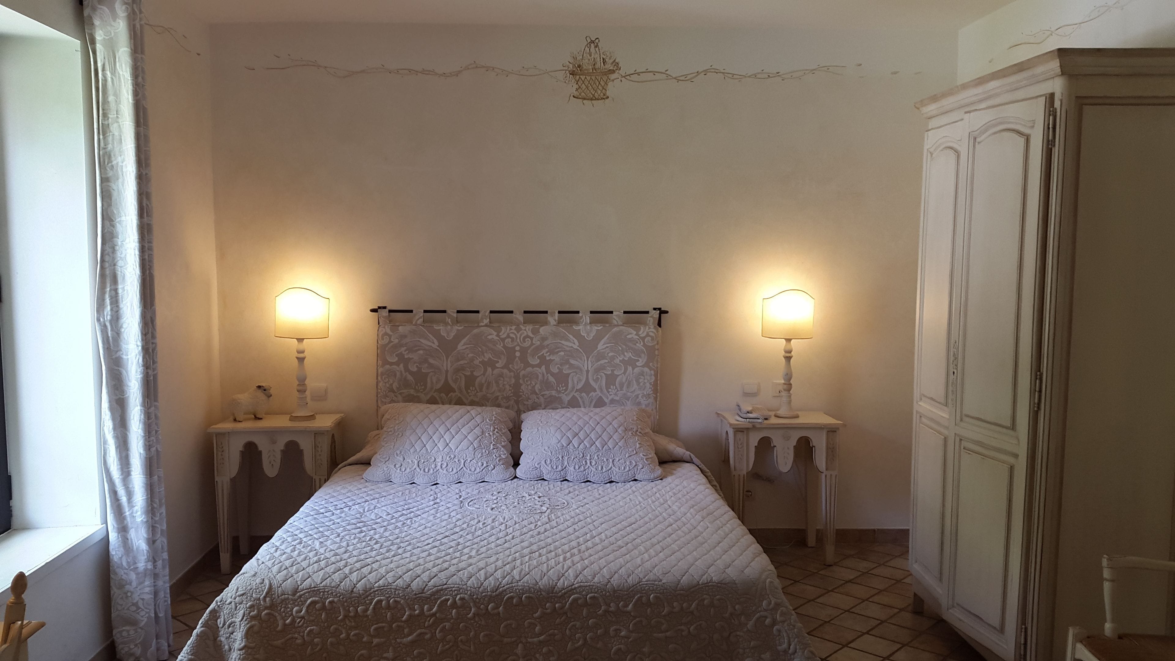 Quarto com cama, duas luminárias de cabeceira, guarda-roupa e janela com cortinas.