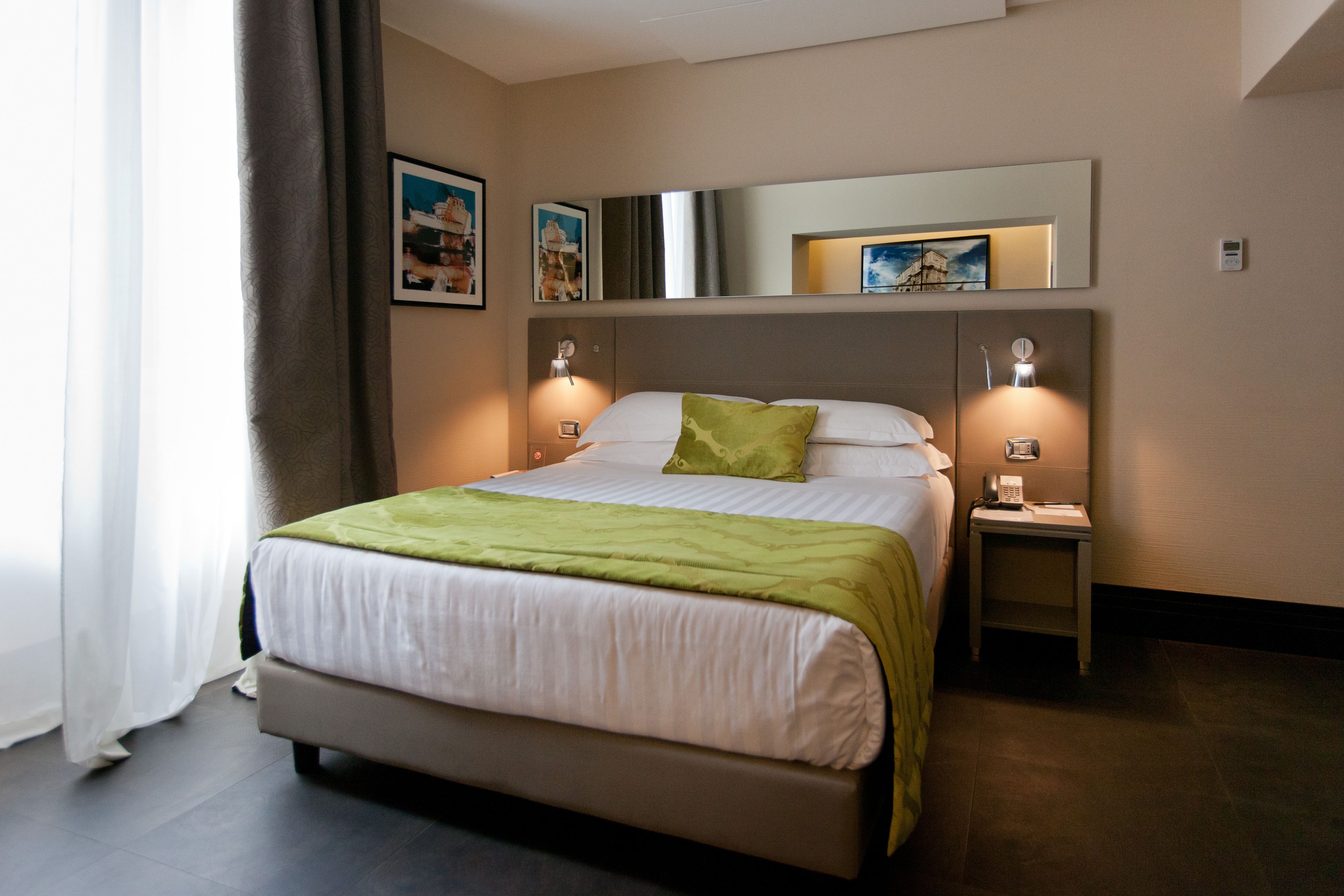 Quarto de hotel com cama, abajures, mesa de cabeceira e uma janela grande com cortinas.