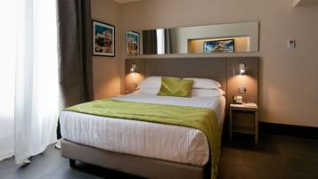 Quarto de hotel com cama, abajures, mesa de cabeceira e uma janela grande com cortinas.