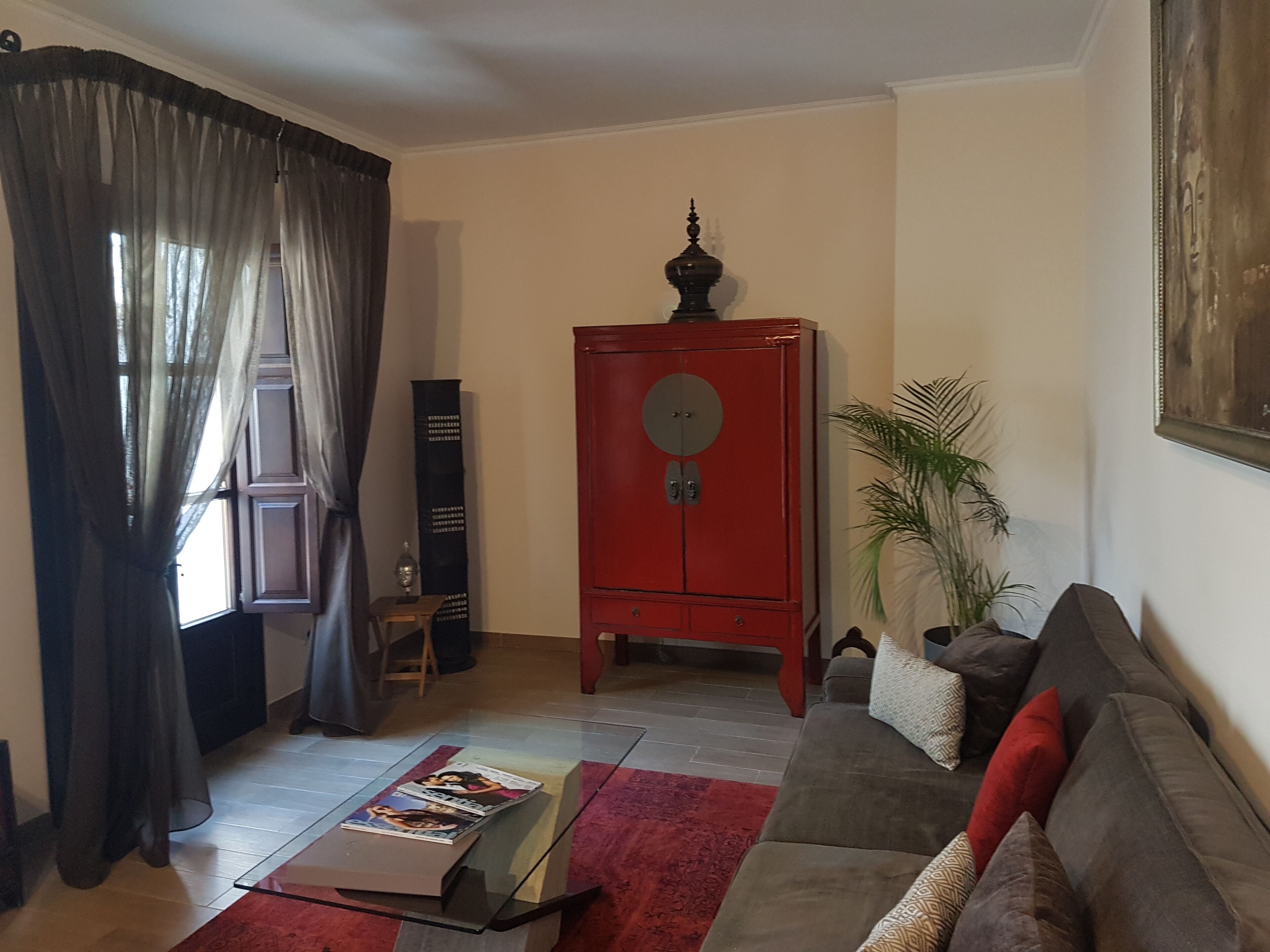 Uma sala de estar com um armário vermelho, um sofá, uma mesa de centro de vidro e um vaso de planta.