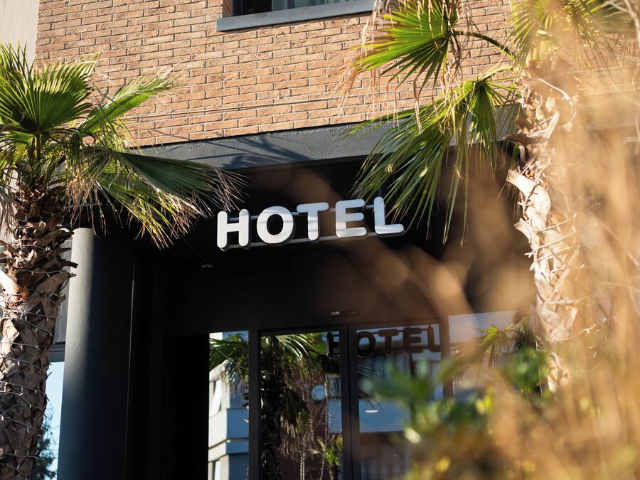 Entrada de hotel com fachada de tijolos, toldo e plantas em vasos.