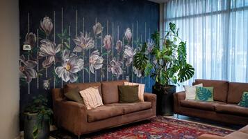 Sala de estar com dois sofás, uma grande planta em vaso, tapete estampado e parede com um mural floral.