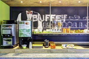 Um balcão de buffet com uma máquina de café, um quadro de menu e diversos alimentos expostos.