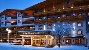 Um hotel com várias varandas, uma árvore coberta de neve e uma placa com a inscrição "JUFA Alpenhotel".