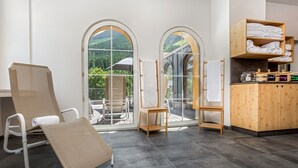 Quarto com uma grande janela, um armário de madeira com toalhas, uma cadeira e uma pequena mesa.
