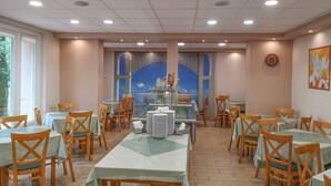 Uma área de refeições com várias mesas e cadeiras, um mural decorativo e um relógio na parede.