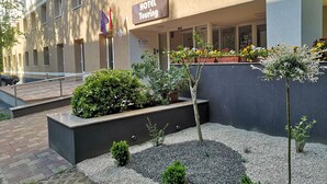 Um hotel chamado "Hotel Touring" com fachada moderna, área de estar externa com plantas em vasos e vista clara da entrada.