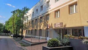 Um hotel com uma placa indicando 'HOTEL Touring' e uma área de entrada pavimentada com um pequeno jardim.