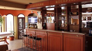 Uma área de recepção com balcão de madeira, banquetas e uma tela de televisão.