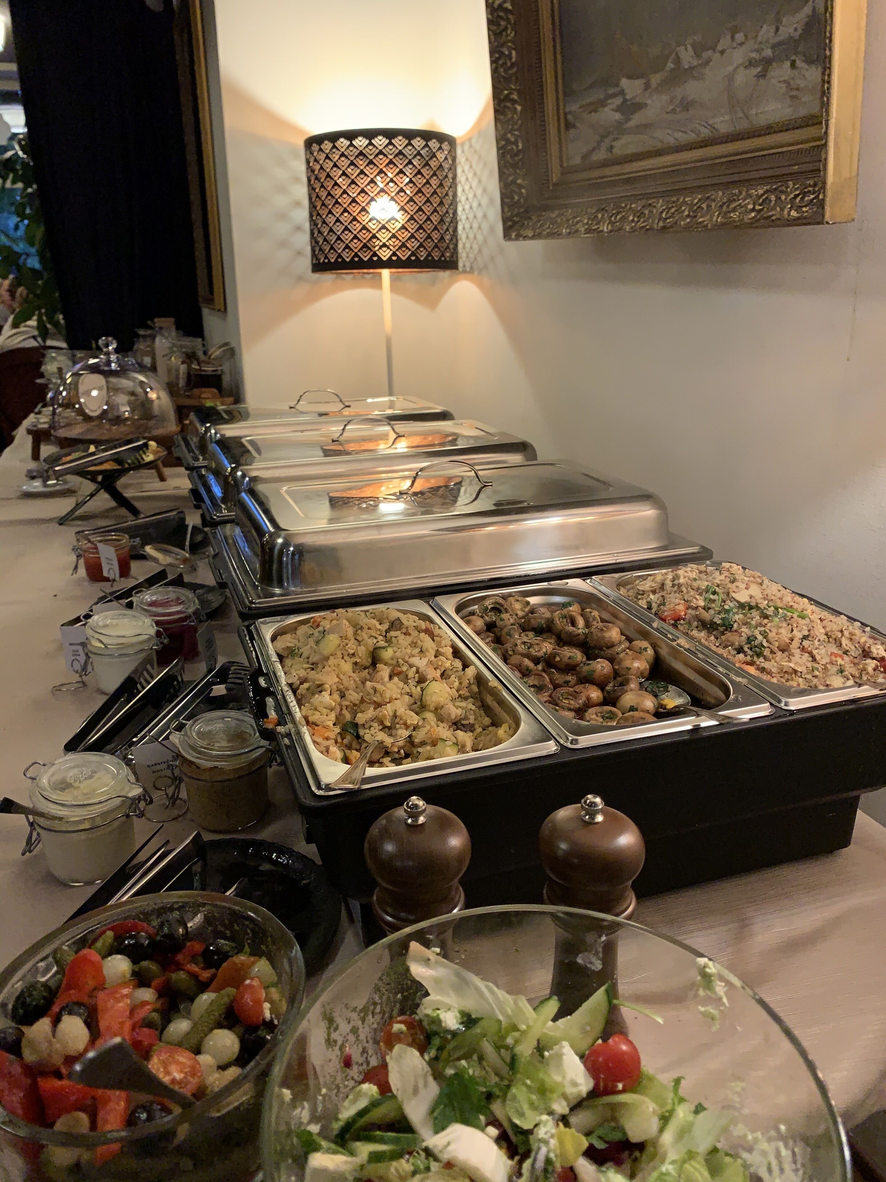 Buffet com diversos pratos, incluindo arroz e saladas, e uma luminária ao fundo.
