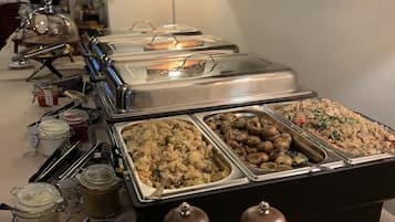 Buffet com diversos pratos, incluindo arroz e saladas, e uma luminária ao fundo.