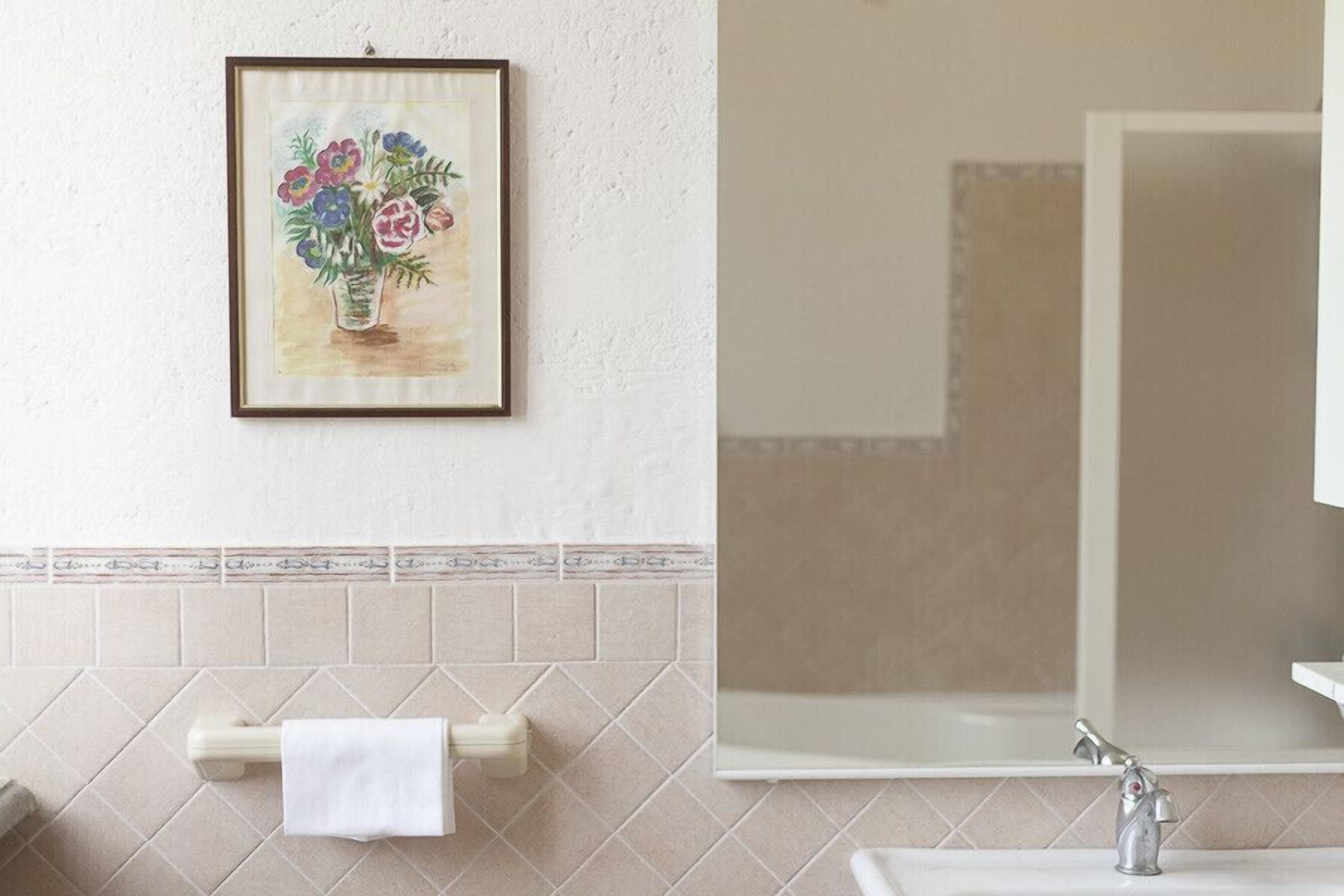 Um banheiro com uma pia branca, um espelho e uma obra de arte floral emoldurada na parede.