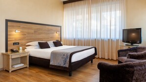 Quarto de hotel com uma cama grande, uma televisão, uma cadeira e uma mesa de cabeceira.