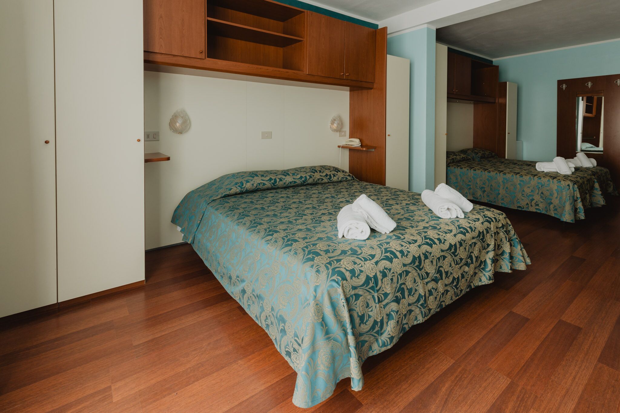 Quarto de hotel com duas camas, soalho em madeira e roupeiro embutido.