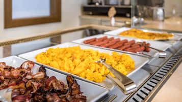 Buffet com diversas opções de café da manhã, incluindo bacon, ovos mexidos e linguiça.
