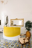 Uma área de recepção com balcão amarelo, espelho, cadeira e planta em vaso.