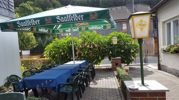 Uma área externa com mesas e cadeiras verdes sob um guarda-sol verde com a inscrição 'Saalfelder'.