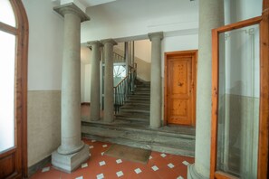 Uma escadaria com colunas, uma porta de madeira e um chão ladrilhado.
