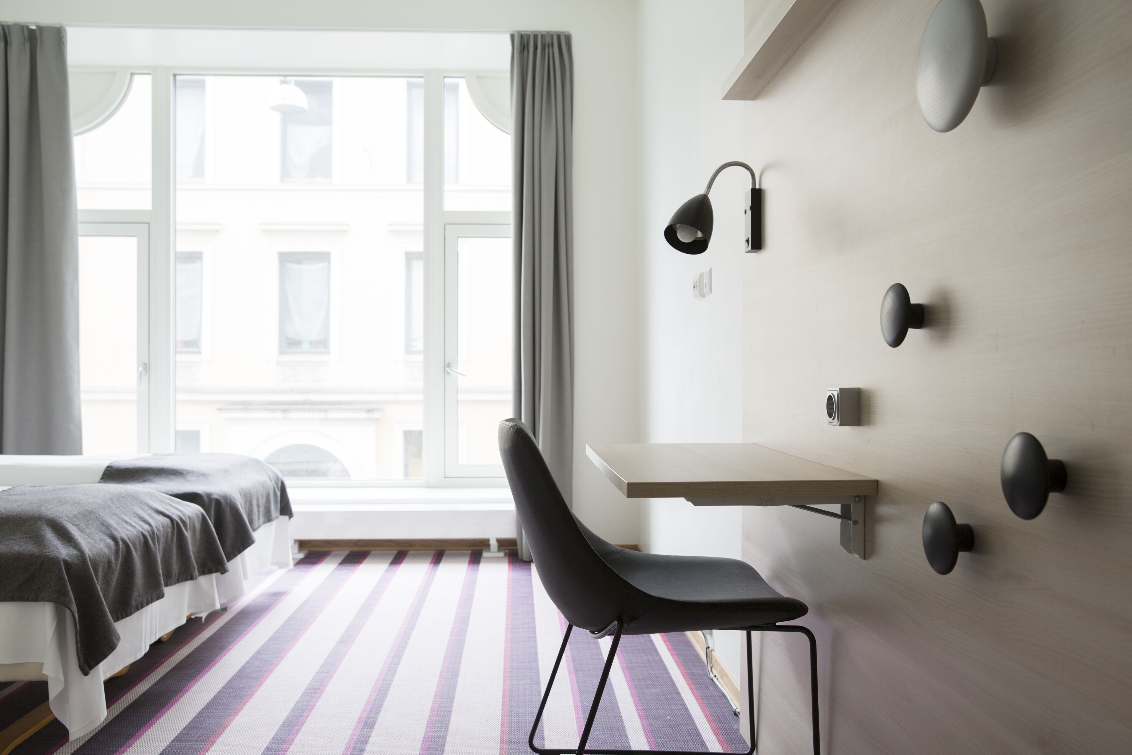 Quarto de hotel moderno com cama, escrivaninha, cadeira e uma grande janela com cortinas.