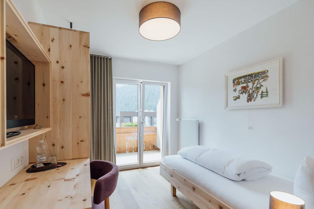 Quarto moderno com escrivaninha de madeira, cadeira roxa, sofá branco e uma janela grande.