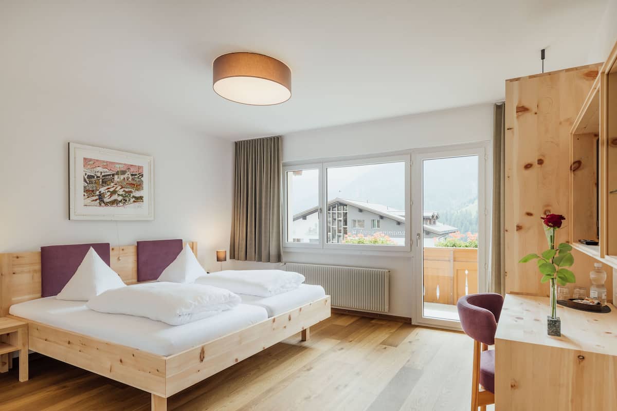 Quarto moderno com cama de madeira, escrivaninha e vista para uma paisagem montanhosa.
