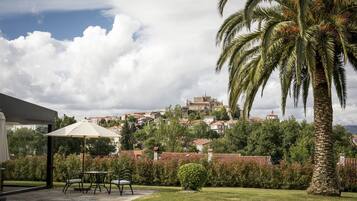 Um pátio com mesa e cadeiras, uma palmeira e vista para uma cidade com edifícios ao fundo.