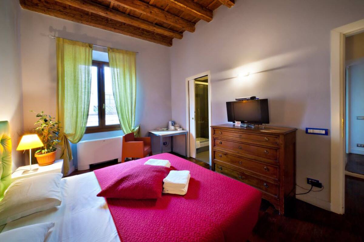 Um quarto com cama, cômoda, escrivaninha, televisão e janela com cortinas.