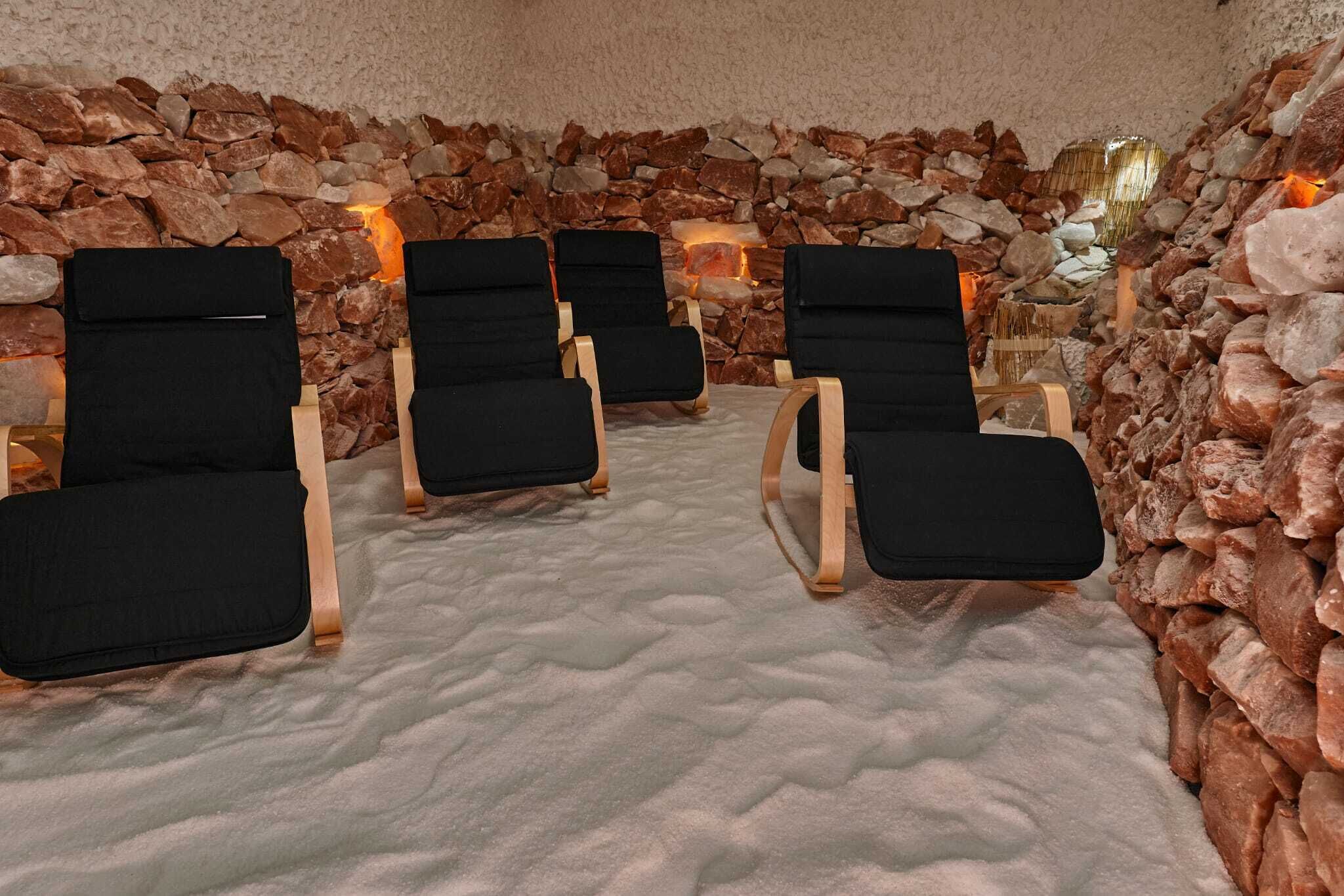 Um quarto com quatro cadeiras pretas, parede de pedra e piso texturizado.