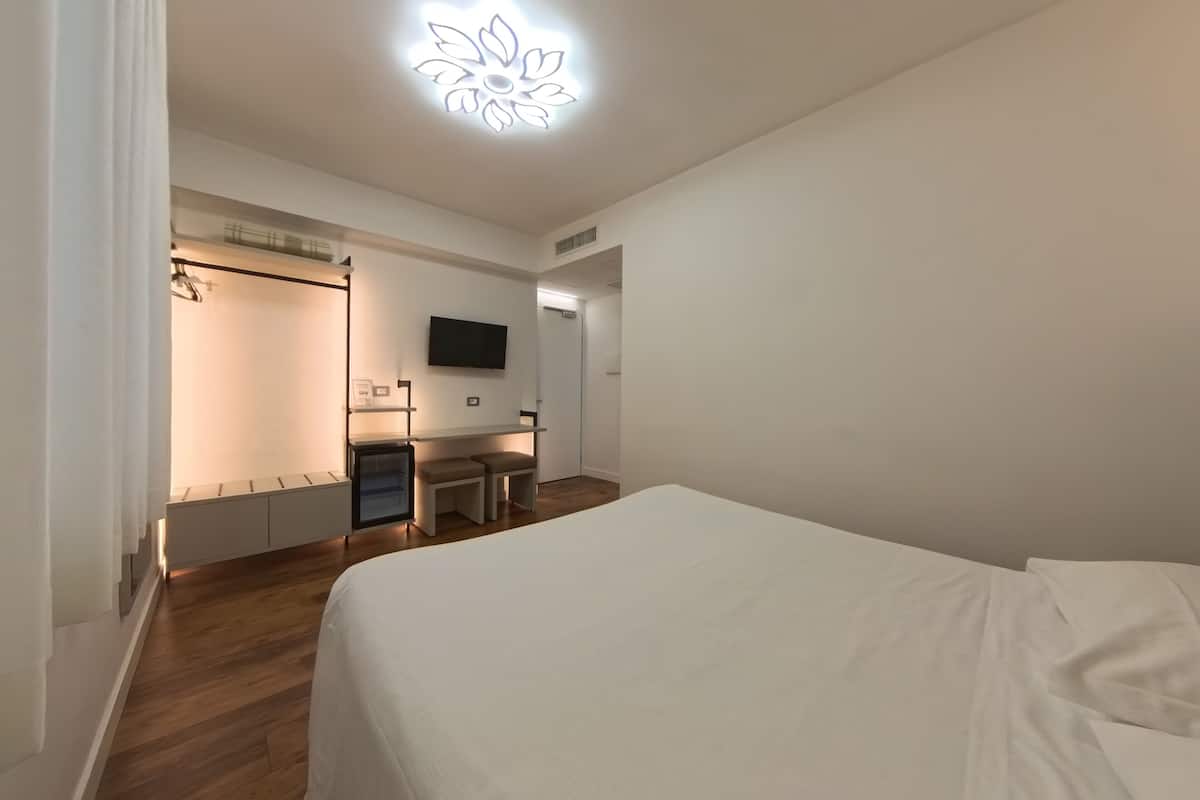 Quarto com cama, escrivaninha com cadeira, televisão e luminária de teto.