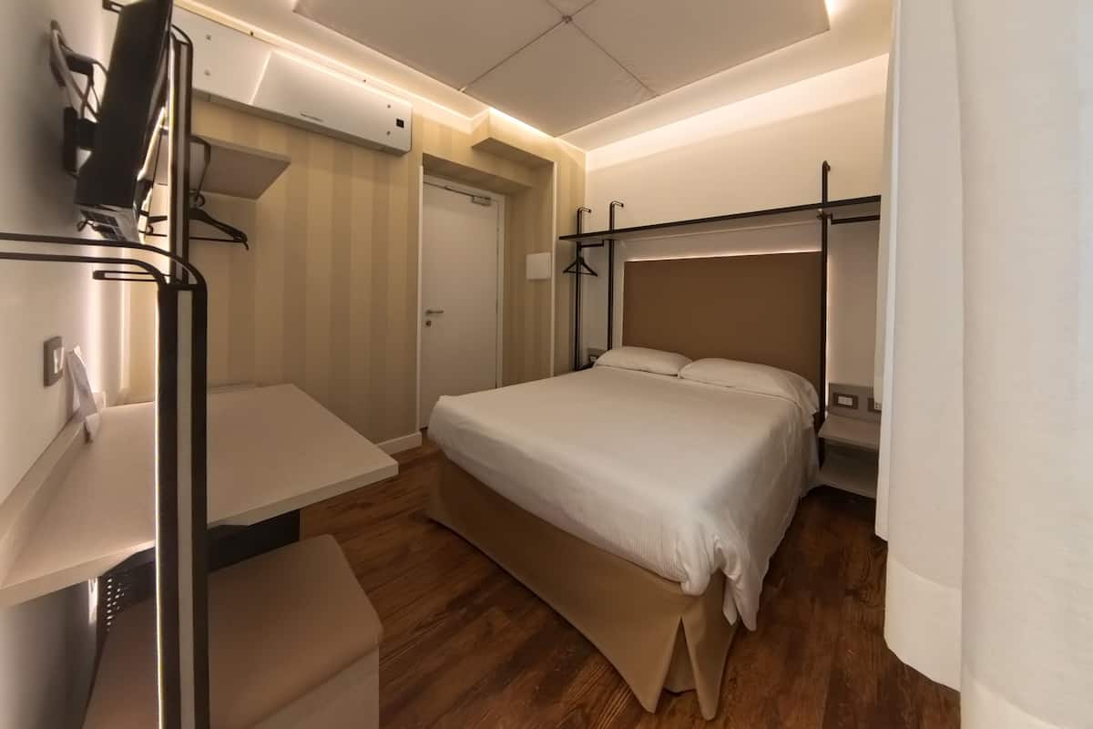 Quarto de hotel com cama, mesas de cabeceira, escrivaninha e guarda-roupa.