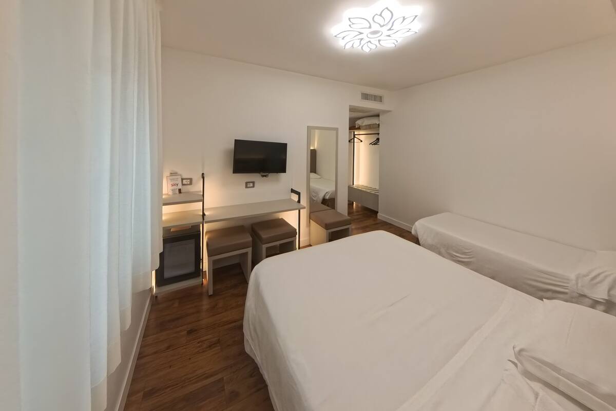 Quarto de hotel com cama, escrivaninha, televisão e guarda-roupa.