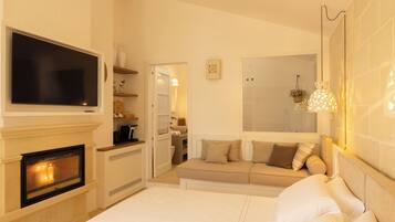 Quarto de hotel com cama, sofá, televisão, lareira e luminária fixada na parede.