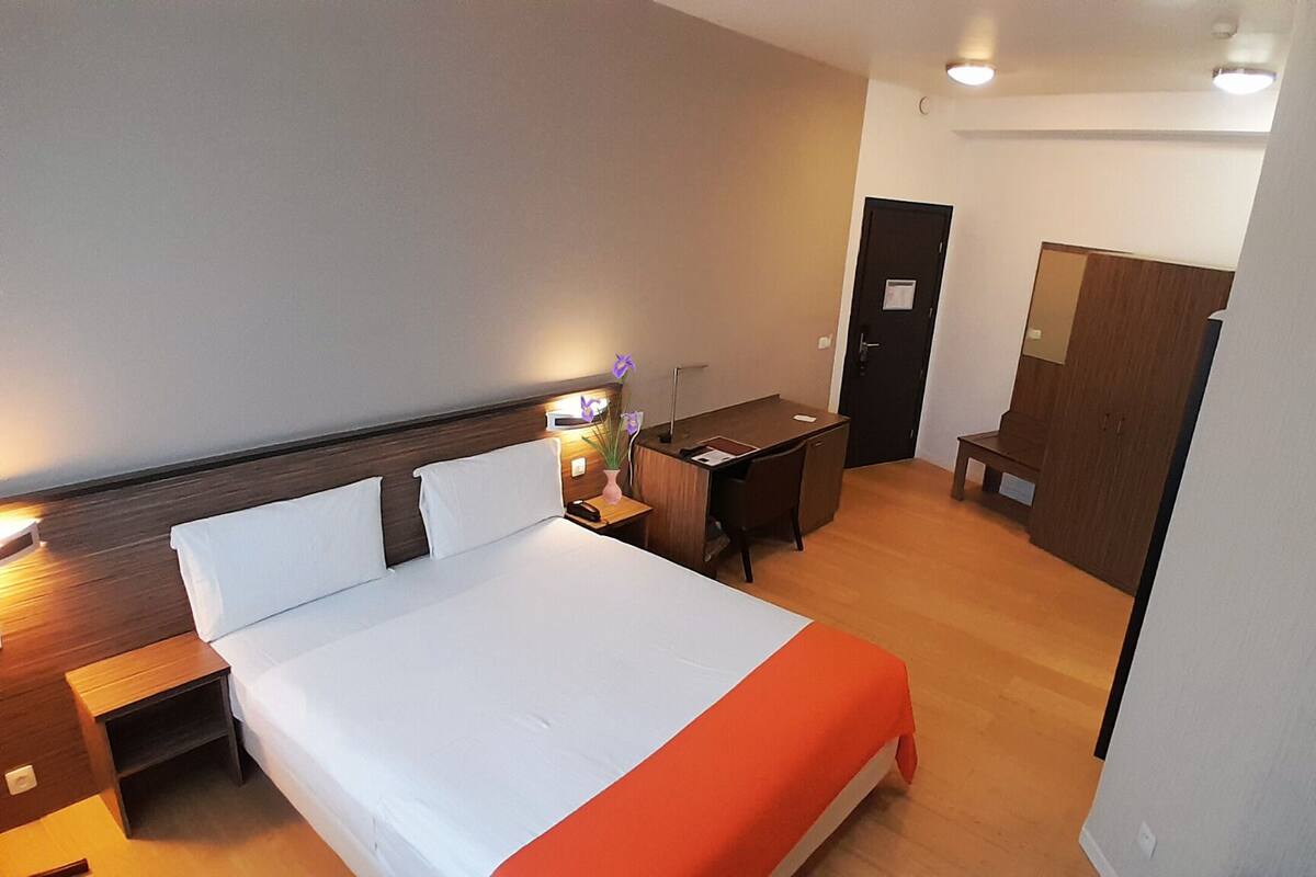 Quarto de hotel com cama, escrivaninha, cadeira e guarda-roupa.