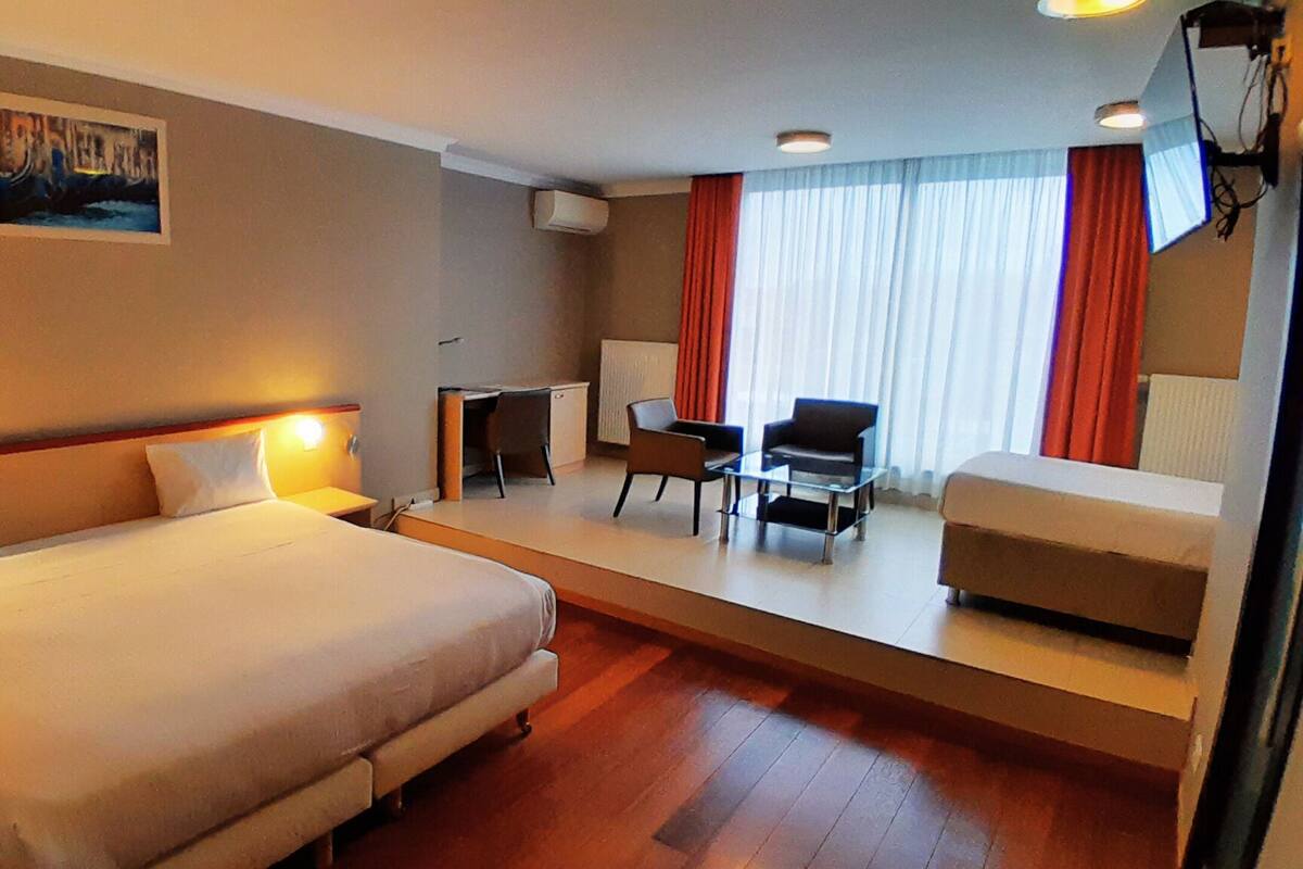 Quarto de hotel com uma cama grande, uma escrivaninha, uma cadeira e um sofá.