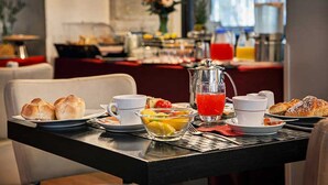 Uma mesa posta para o café da manhã, com pão, frutas, suco e doces.