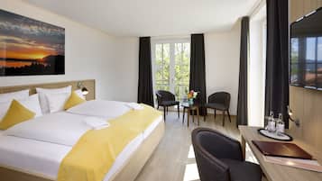 Quarto de hotel com uma cama, uma mesa de escritório, duas cadeiras, uma televisão e uma janela com cortinas.