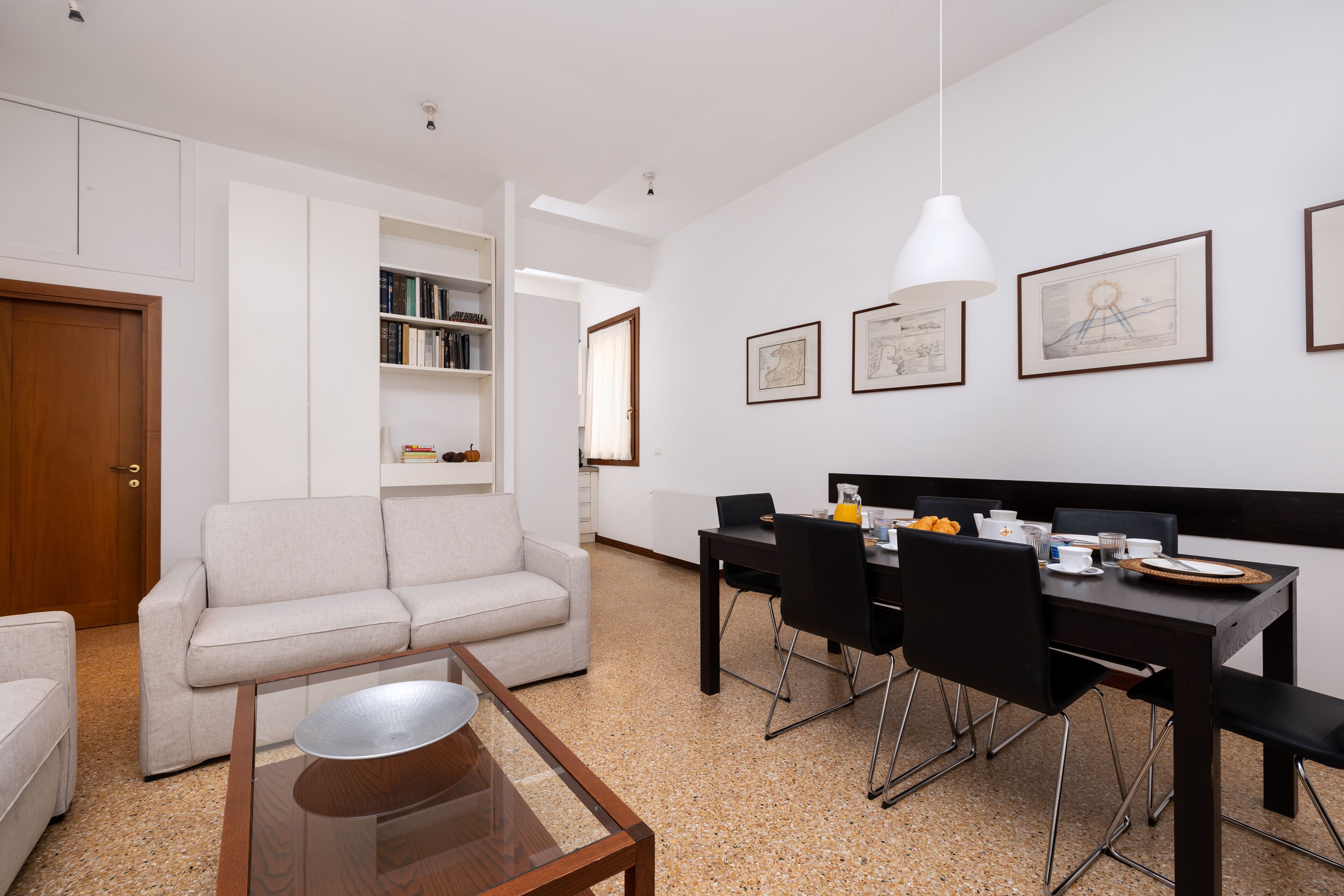Uma sala de estar moderna com sofá, mesa de jantar com cadeiras e área de cozinha com armários e geladeira.