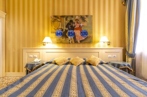 Quarto de hotel com uma cama grande, duas mesas de cabeceira, um quadro na parede e uma cortina na janela.