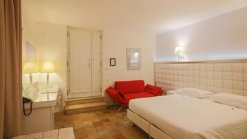 Quarto de hotel com uma cama, uma cadeira vermelha, uma escrivaninha com abajur e um guarda-roupa.