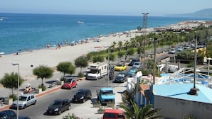 Uma estrada costeira com carros estacionados e uma praia ao fundo.