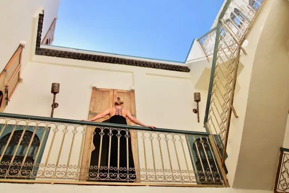 Um edifício com vários níveis, varandas, uma escadaria e céu azul visível pelas janelas.
