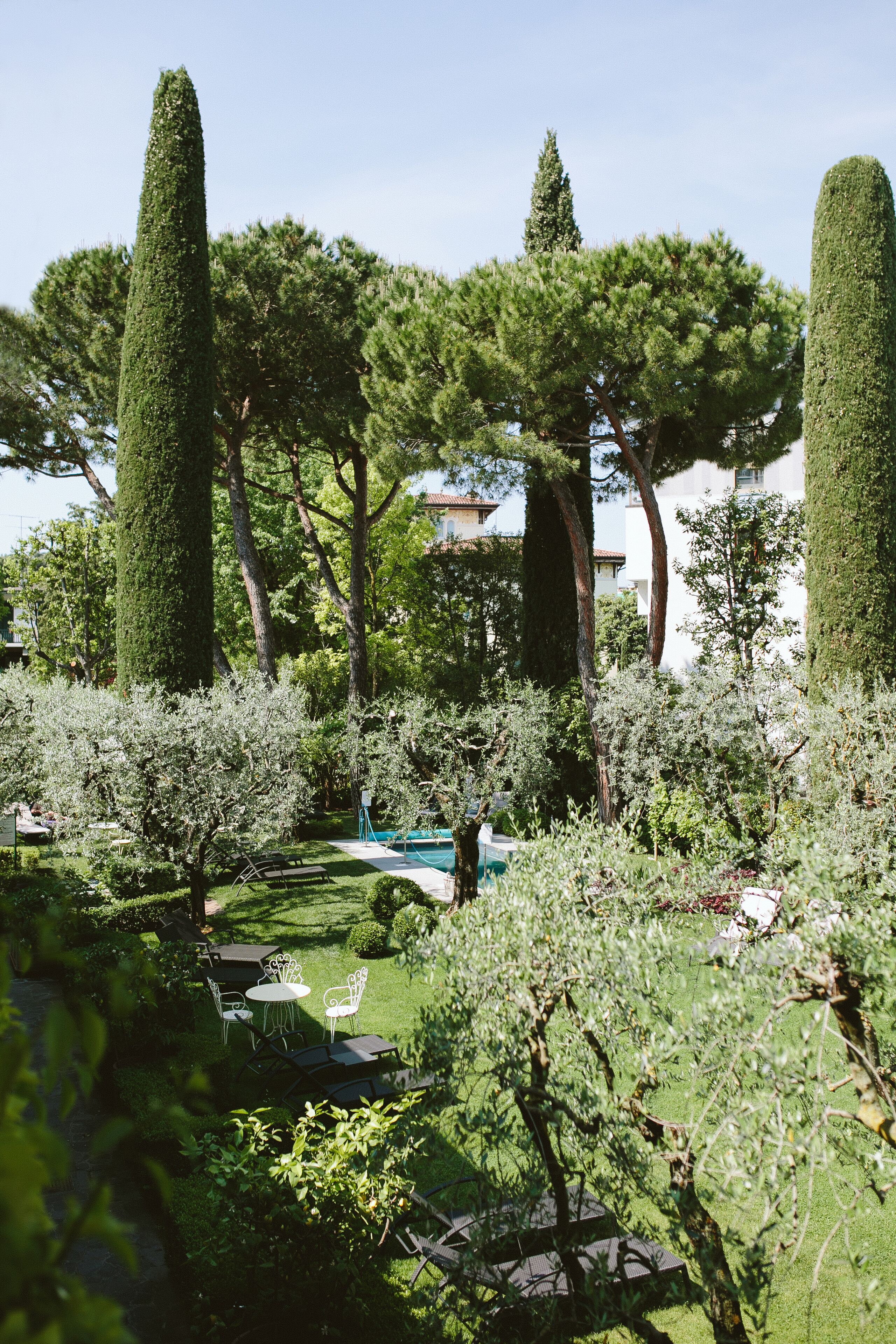 Um jardim bem cuidado com piscina, mobiliário de exterior arrumado e árvores altas.